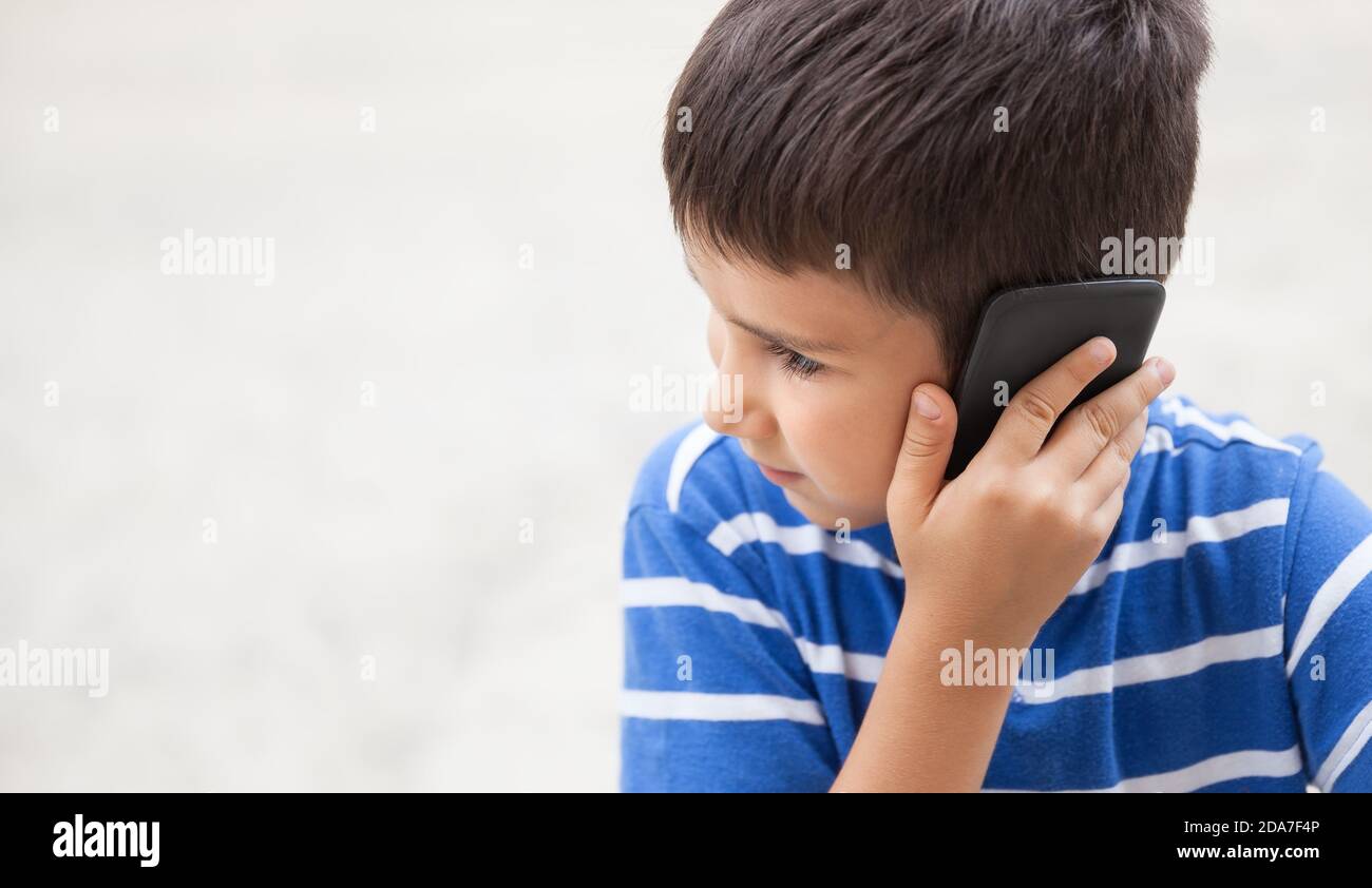 Serious little boy talking on the phone with his parents on light ...