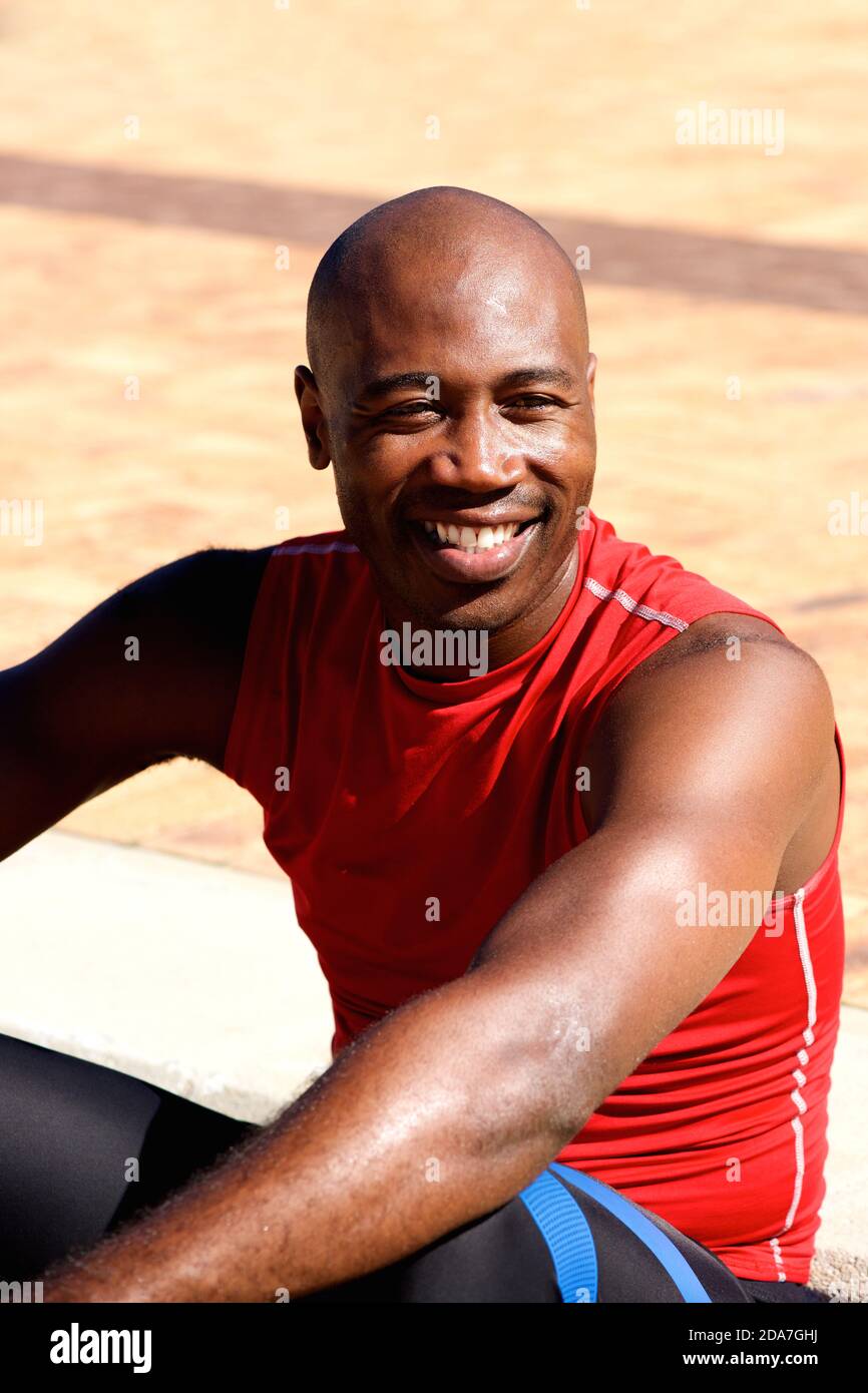Close up portrait of relaxed young african sports man sitting outdoors ...