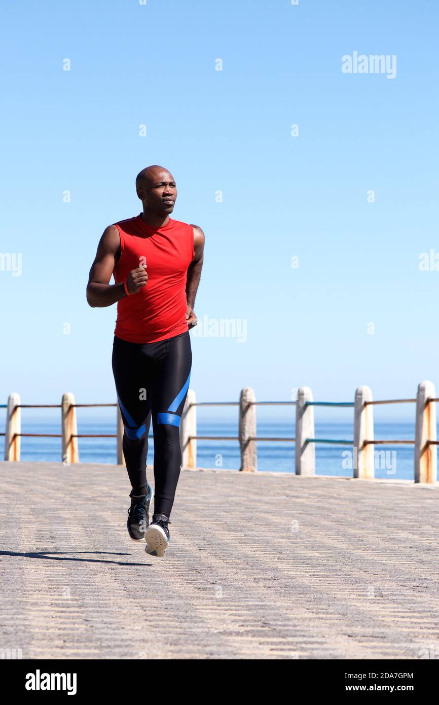 Full length portrait of fit african man jogging on seaside promenade ...