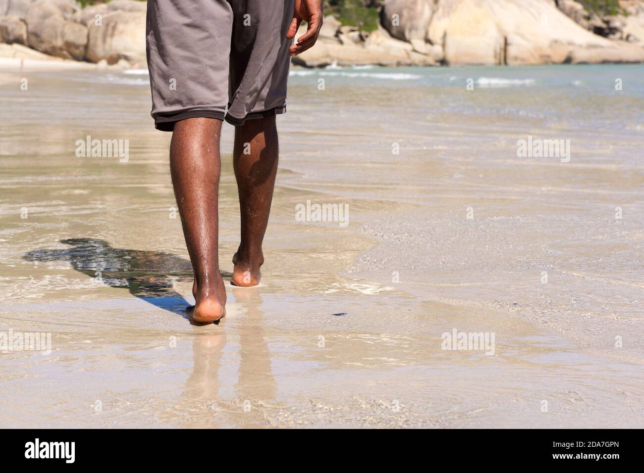 Close up rear view of young man walking with bare feet on the seashore ...