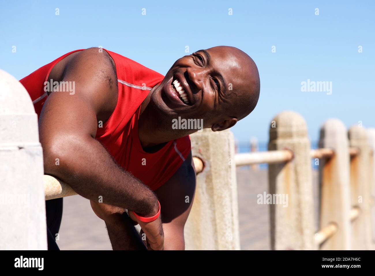 Close up portrait of cheerful young sports man leaning on railing ...