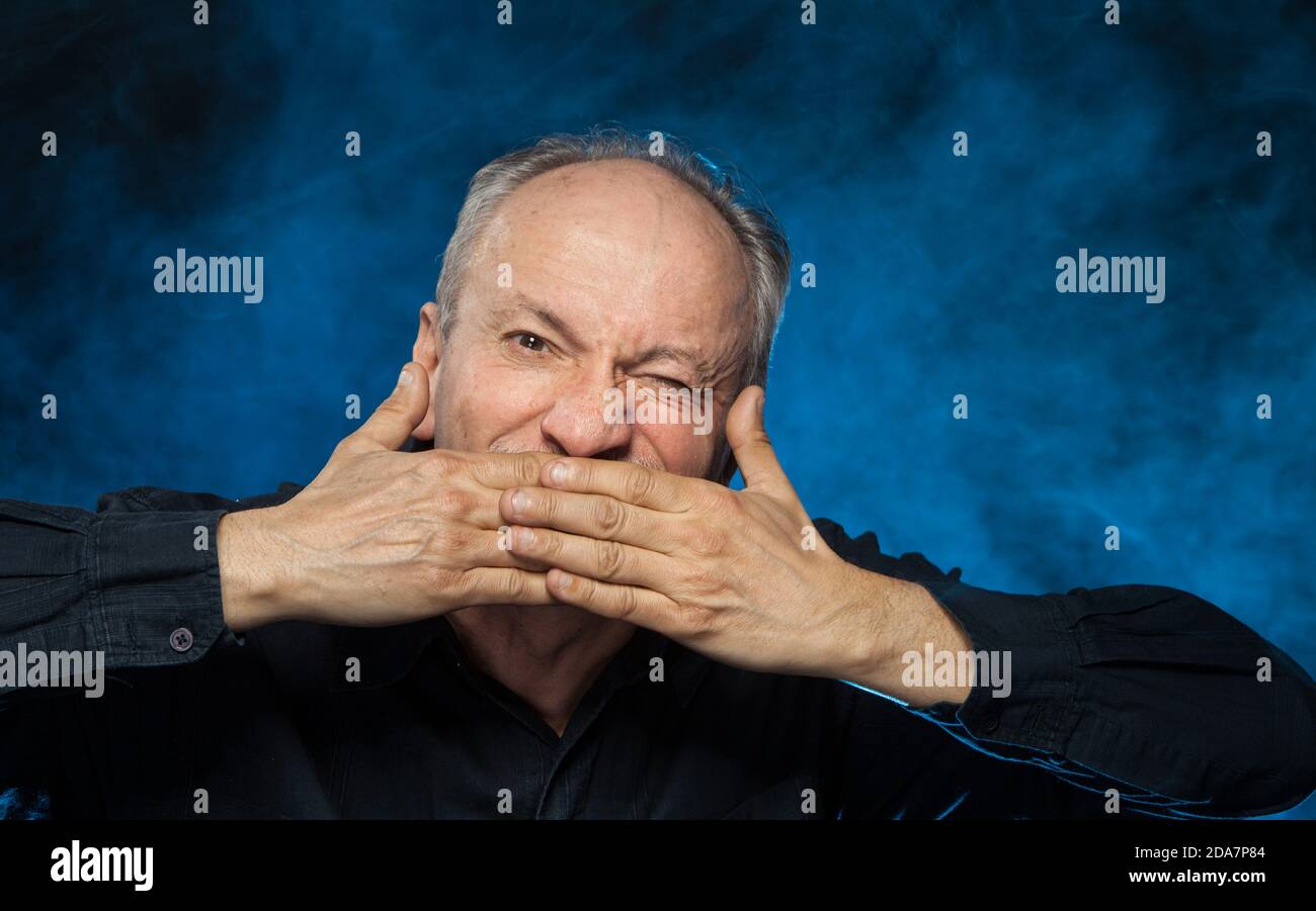 Old macho man. An elderly man covers his mouth with his palms. Portrait ...
