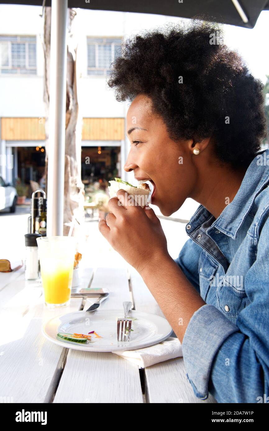 Side portrait of a young african woman eating sandwich at cafe Stock ...