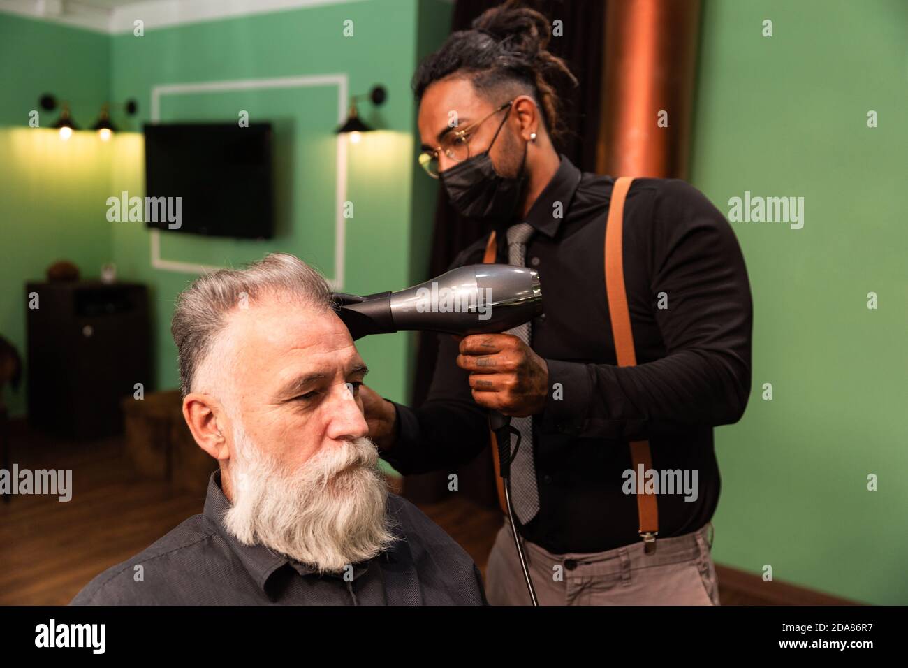 Young African-American tattooed barber combs and blow-drys the hair of ...