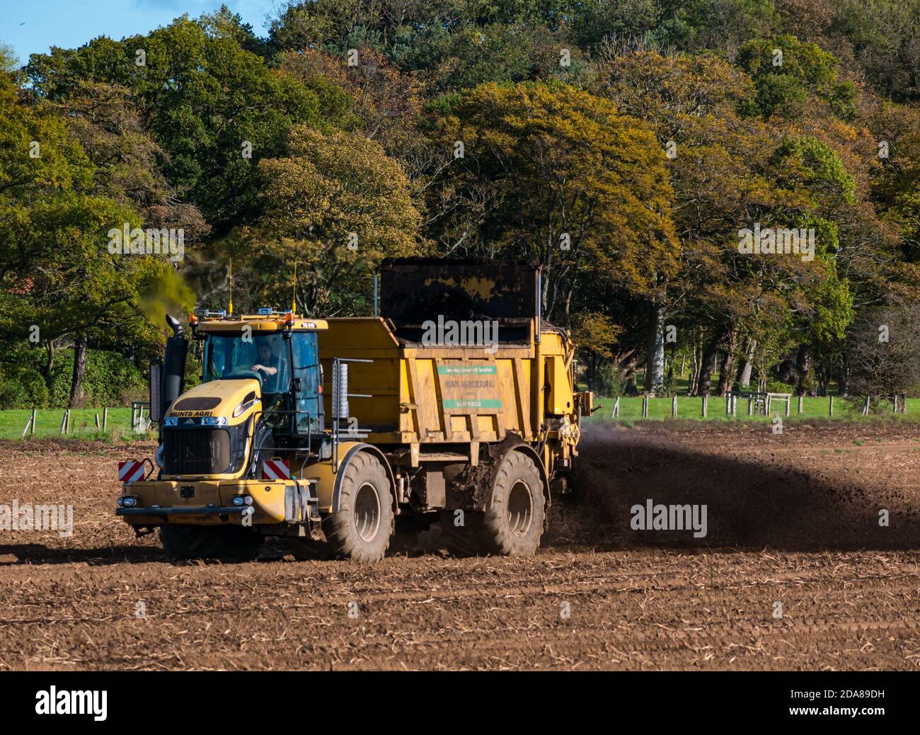 Farm vehicle spreading slurry in field after harvest, East Lothian ...