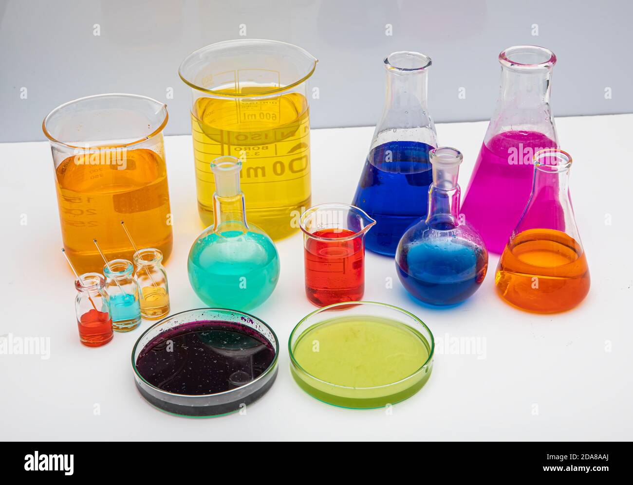 Laboratory glassware with liquids of different colors on white table ...