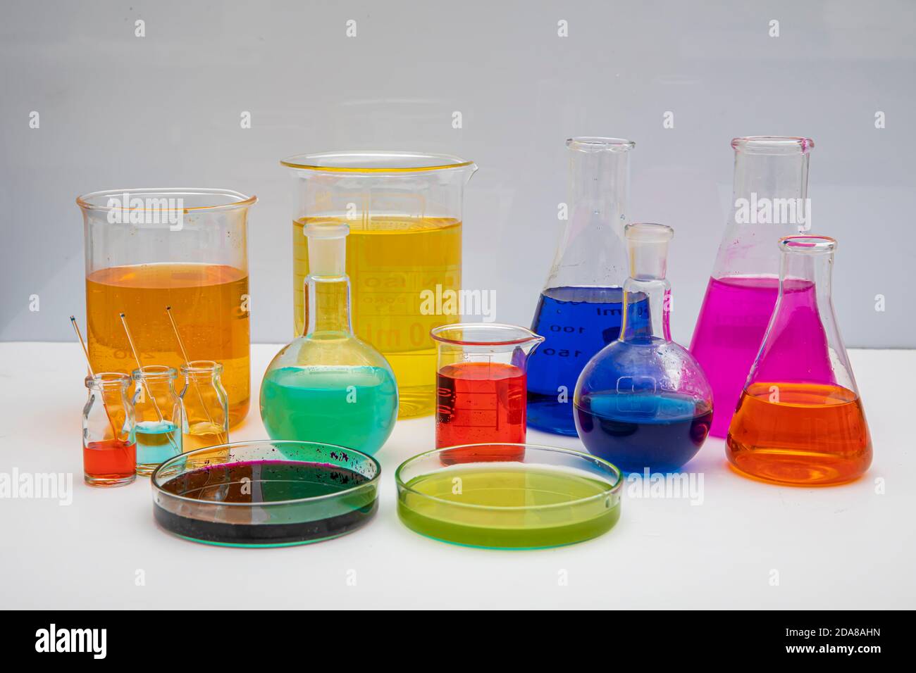 Laboratory glassware with liquids of different colors on white table ...