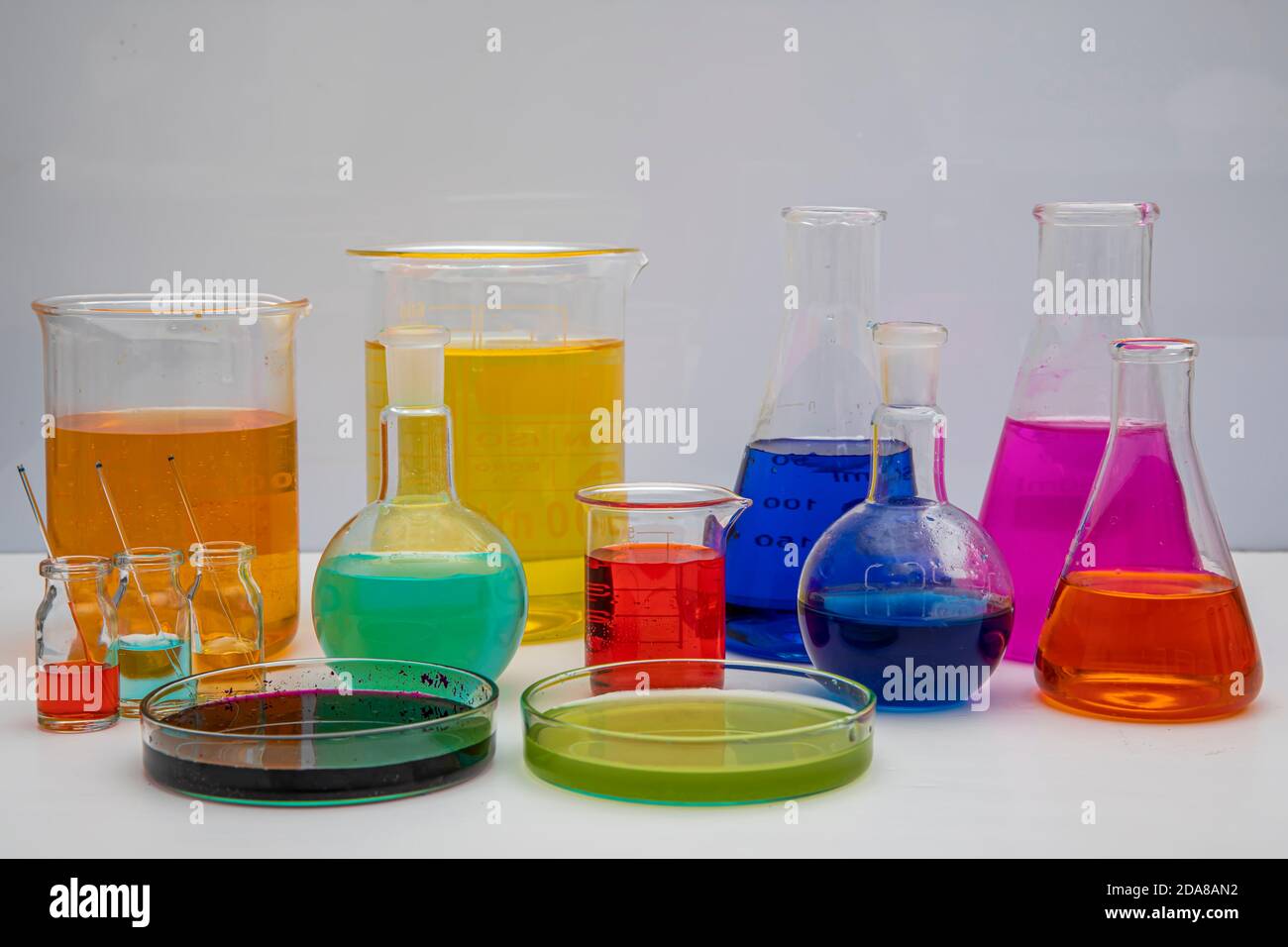 Laboratory glassware with liquids of different colors on white table ...