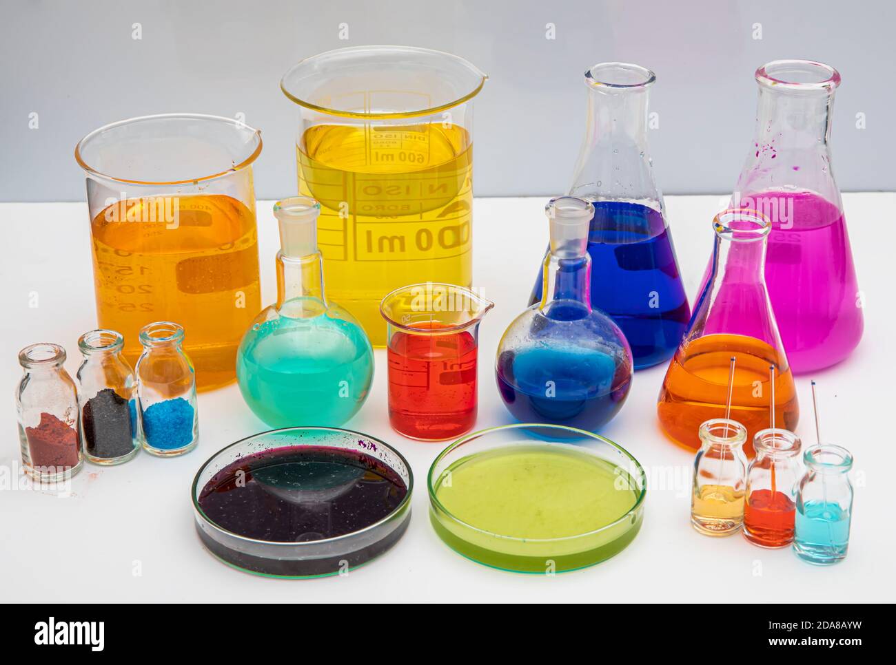 Laboratory glassware with liquids of different colors on white table ...