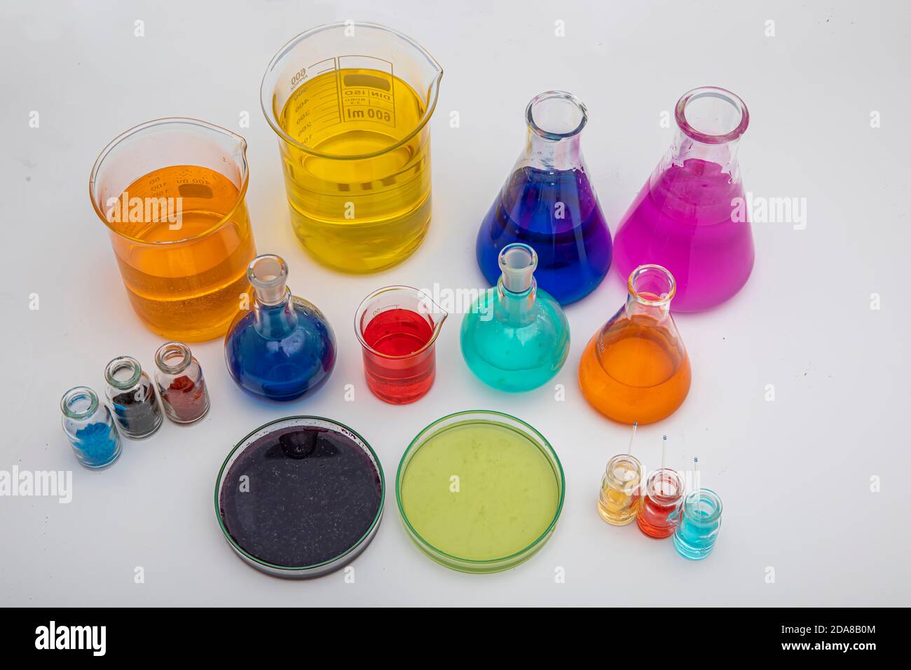 Laboratory glassware with liquids of different colors on white table ...