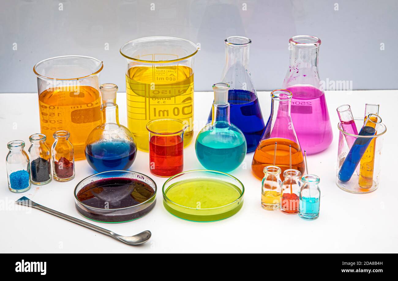 Laboratory glassware with liquids of different colors on white table ...