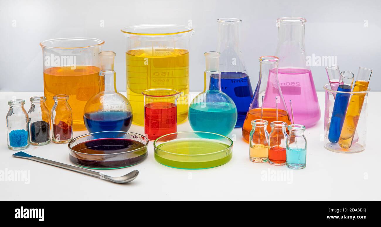 Laboratory glassware with liquids of different colors on white table ...