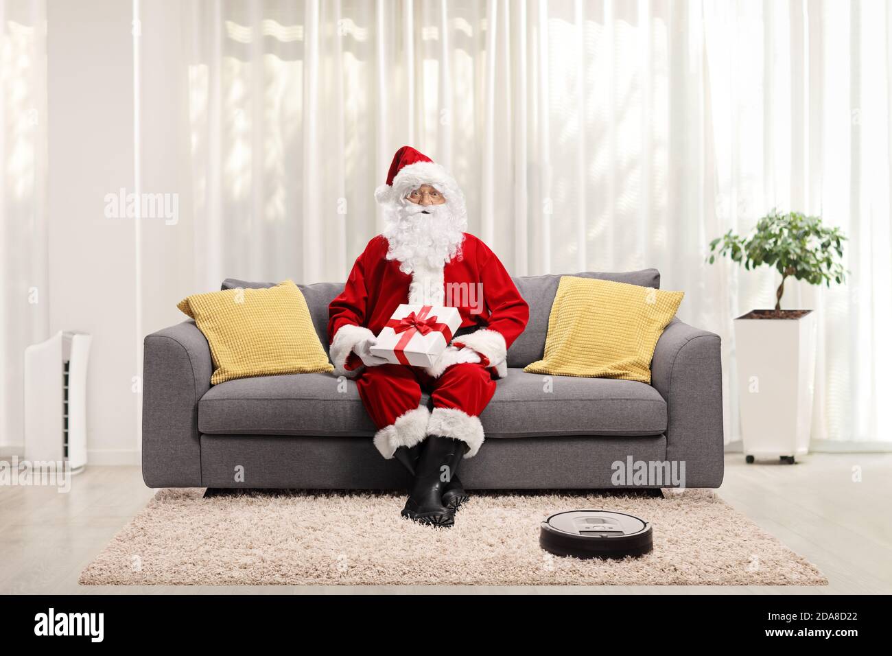 Santa claus sitting on a sofa with a gift box and a robotic vacuum ...