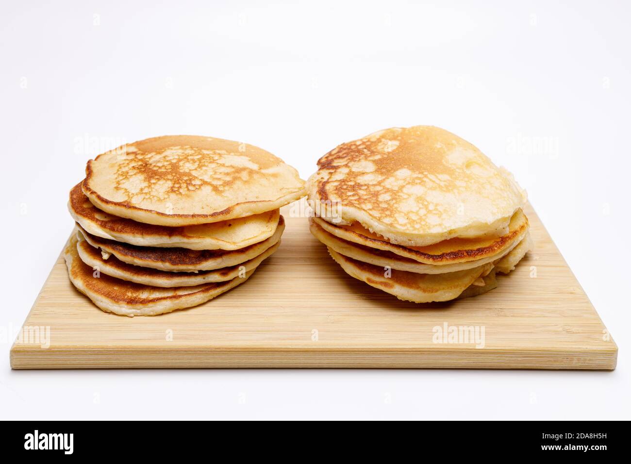 Two stacks of homemade pancakes on a bamboo cutting board on white ...