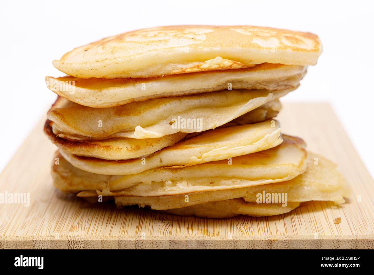 Side view of a pile of pancakes on a bamboo cutting board on uniform ...