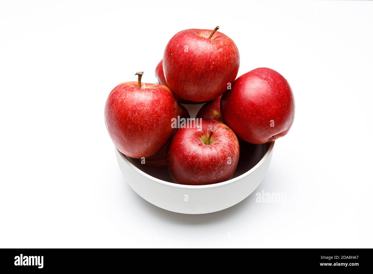 Four red apples in a white ceramic bowl on a white and uniform ...