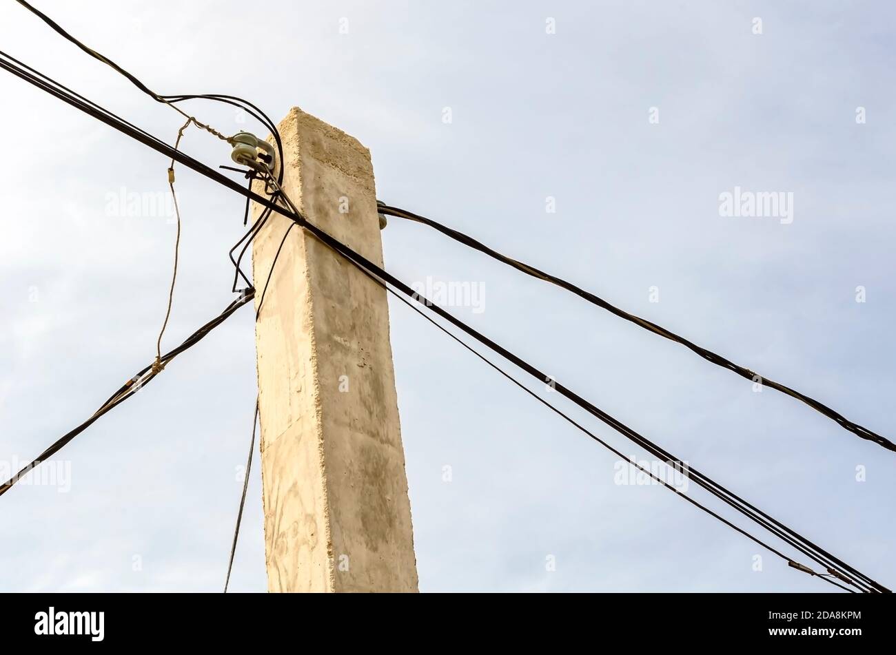 Reaching to the cloudy sky is a square utility post with electric power ...