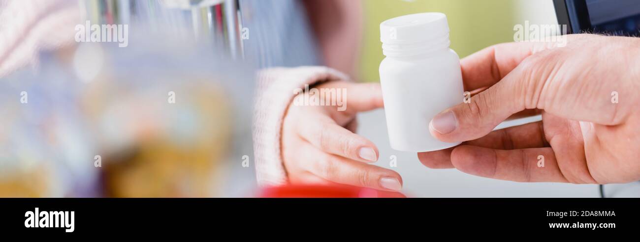 partial view of pharmacist giving bottle with medication to customer ...