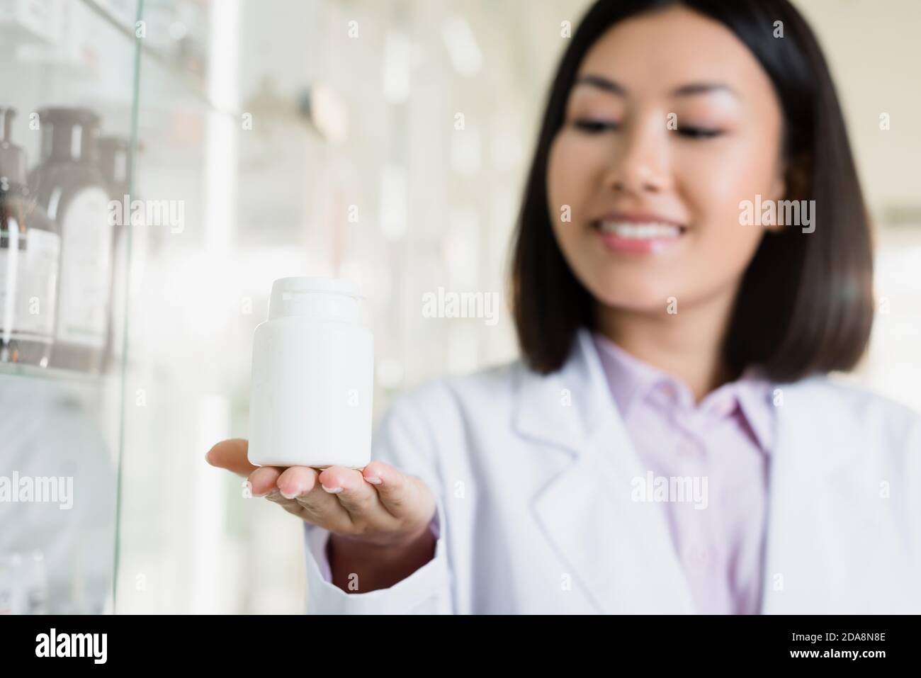 bottle with medication in hand of cheerful asian pharmacist on blurred ...