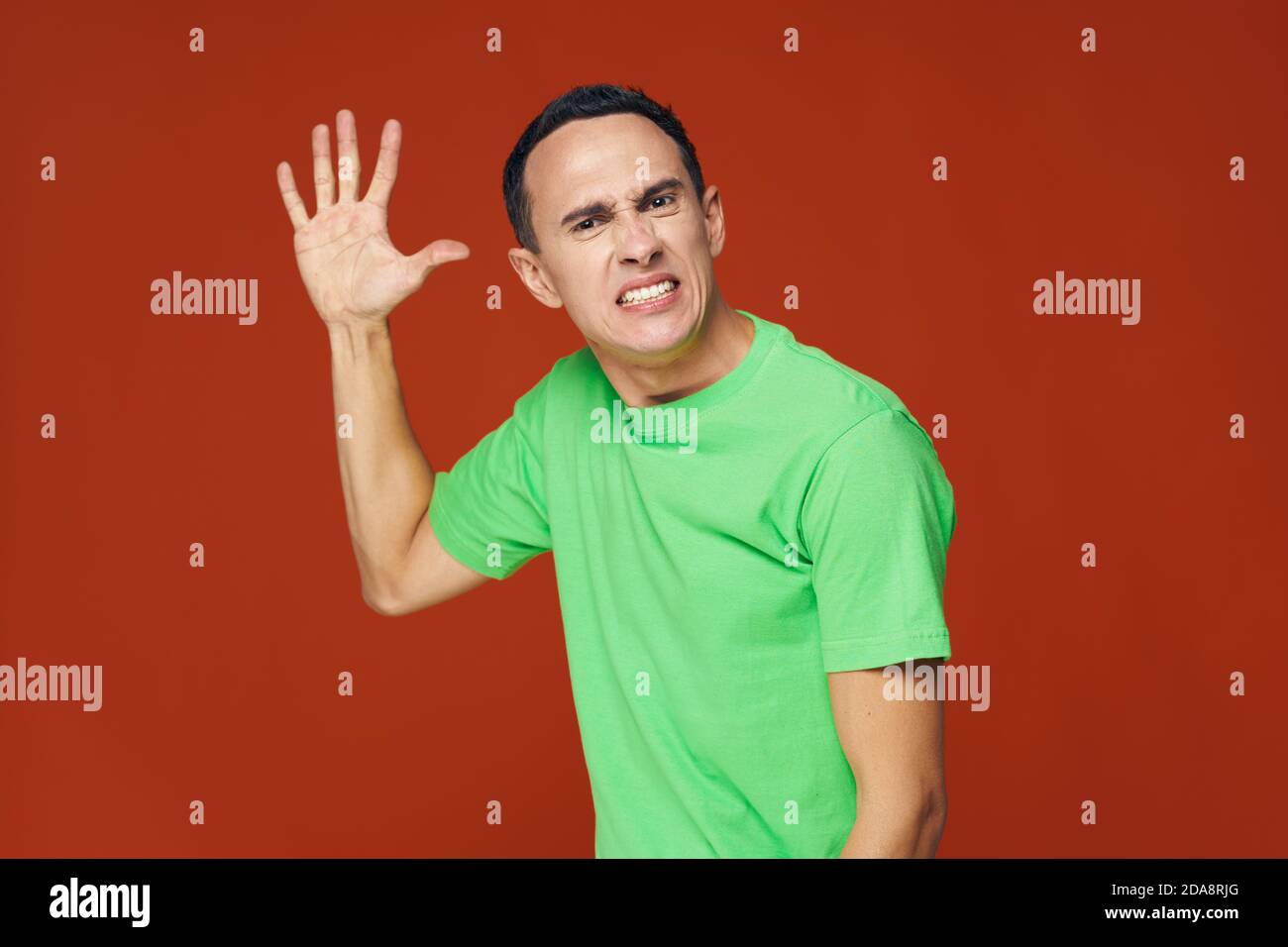 Irritable man gesturing with his hands on a red background in a green t ...