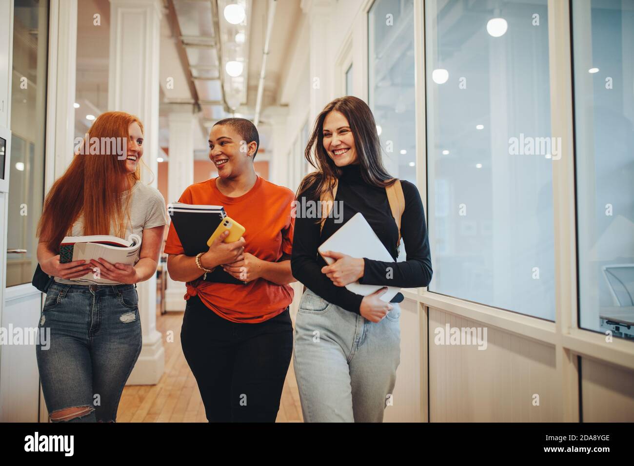 Smiling girls walking through high school corridor after their class ...
