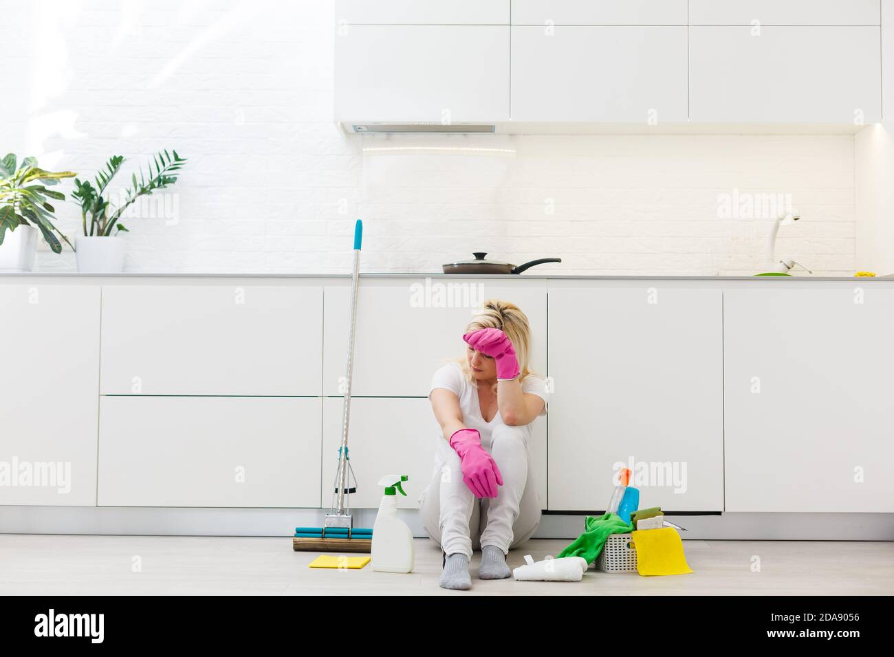 Tired young cleaning lady resting in the kitchen after house keeping ...