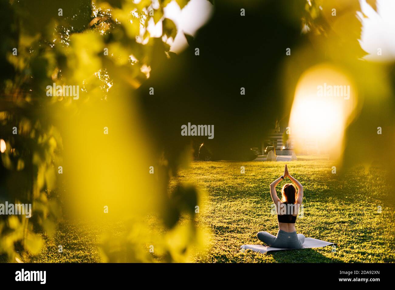 Back view of flexible woman raising arms up and folding them together ...