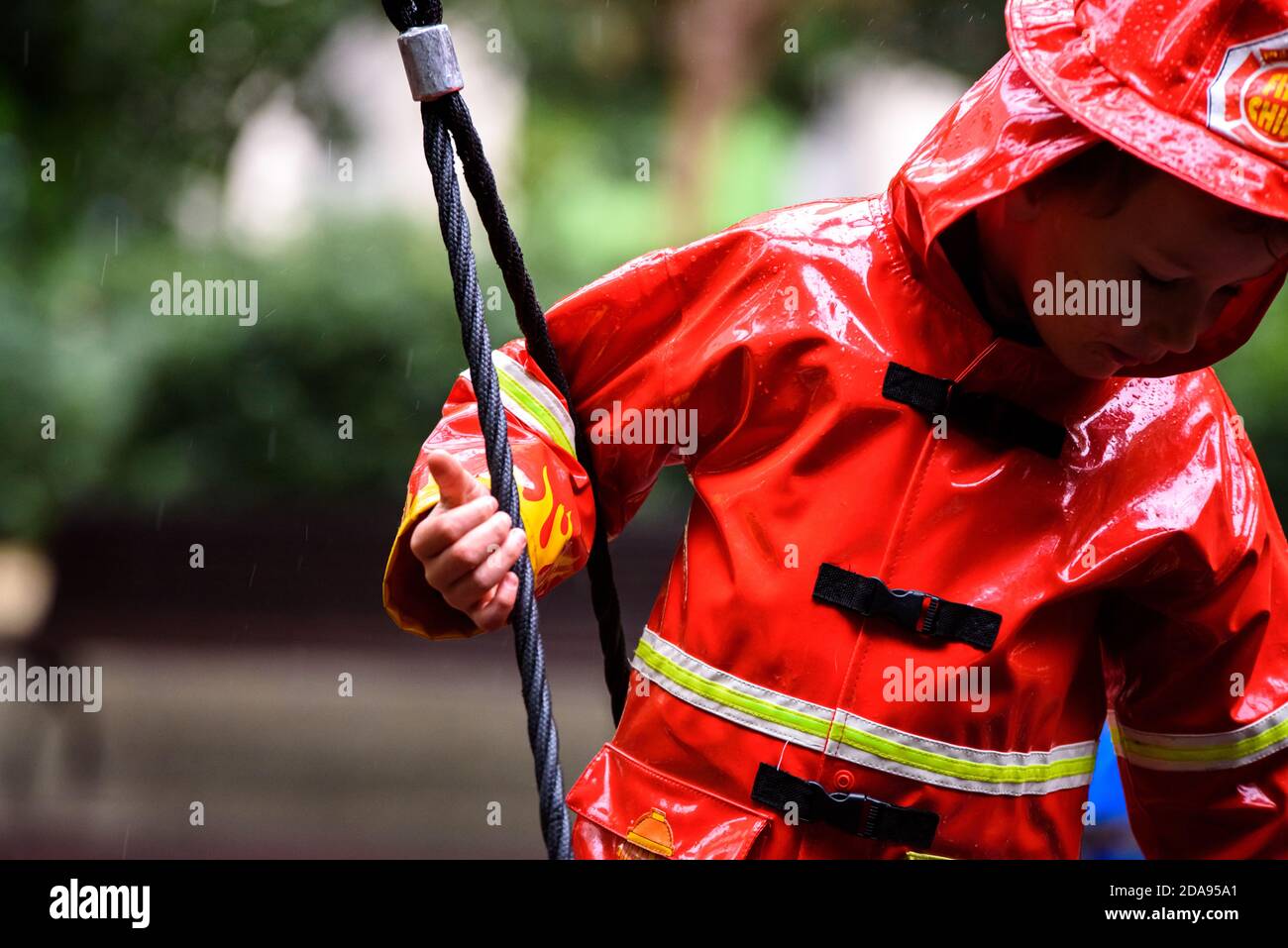 Child with red raincoat of firefighter clings to a rope in a playground ...