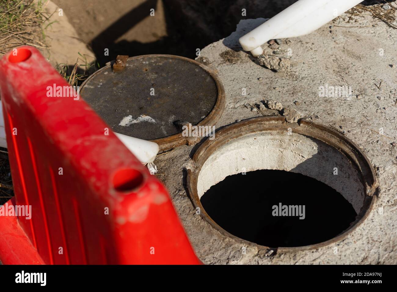 Dangerous open hatch without cover and a warning fence on the road ...