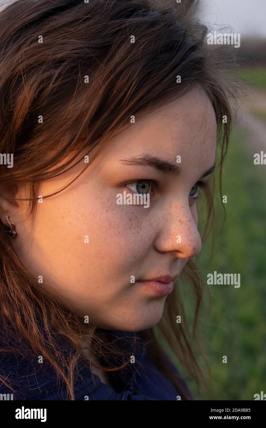 Girl face with freckles on the side against the background of green and ...