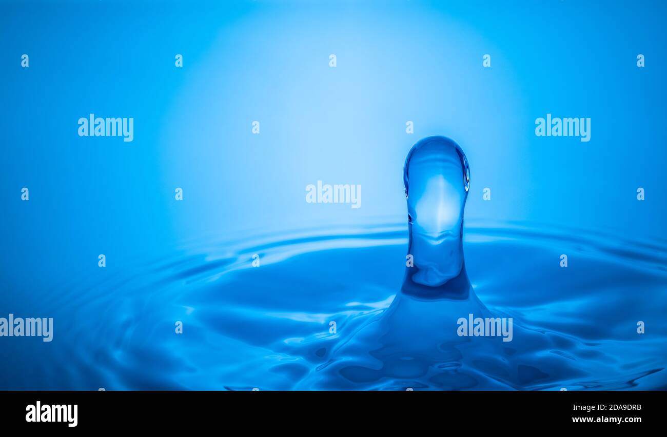 Water drop splashing into blue water surface Stock Photo - Alamy