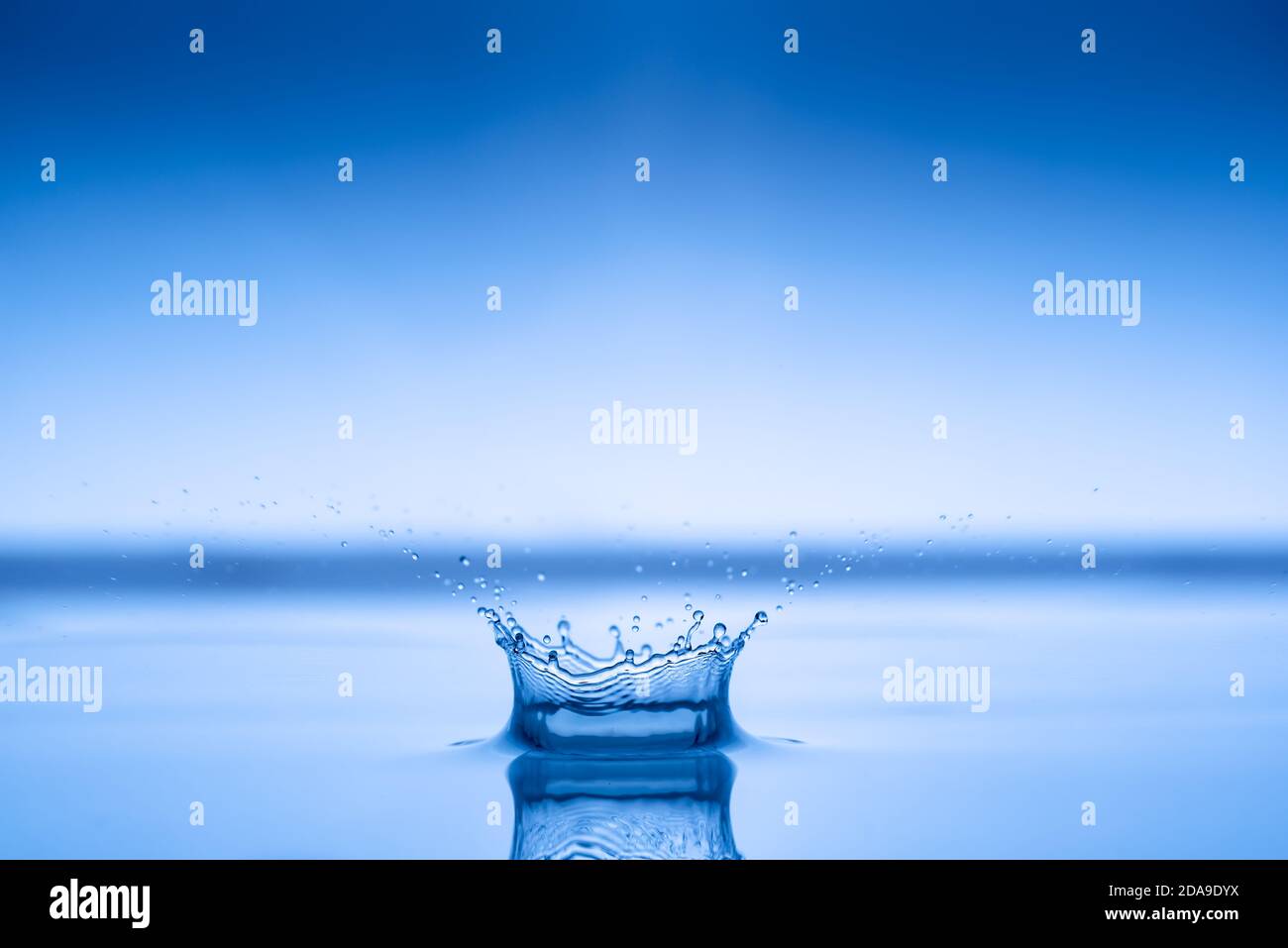 Water drop splashing into blue water surface Stock Photo - Alamy