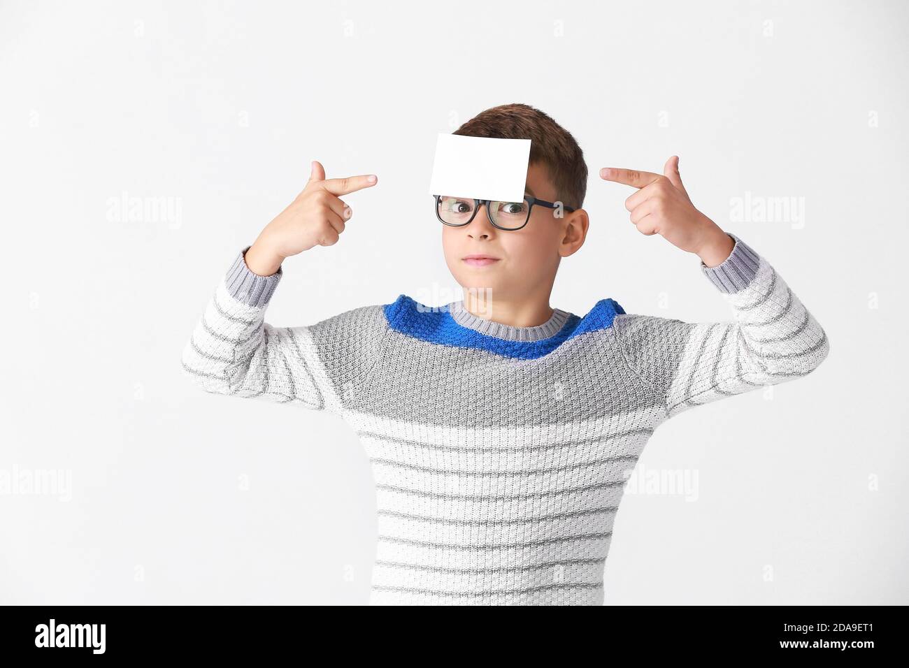 Boy with blank note paper on his forehead against light background ...