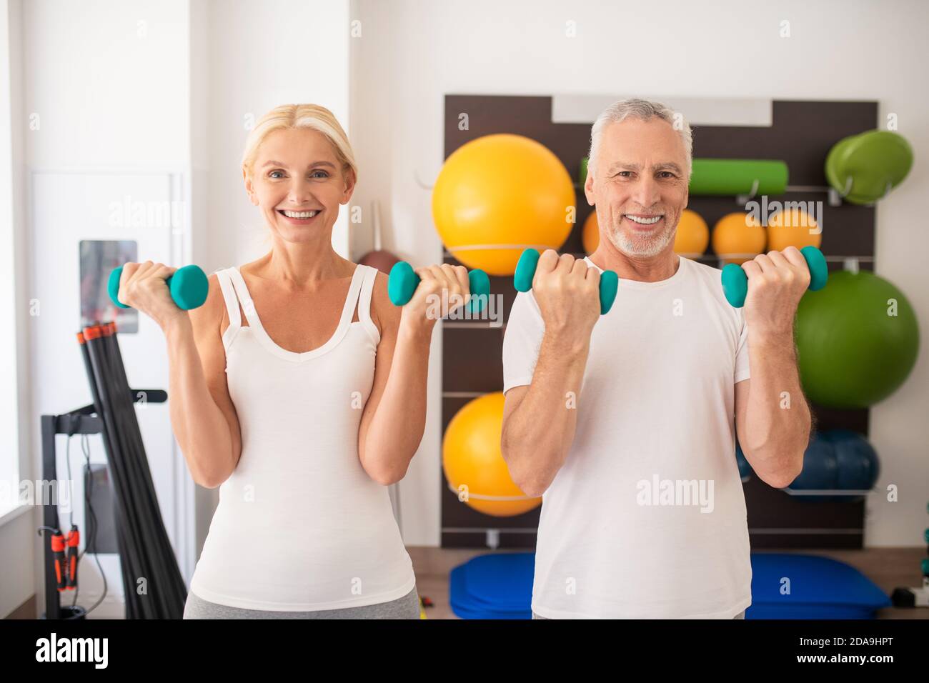 Positive man and woman exercising with dumbbells in the gym Stock Photo ...