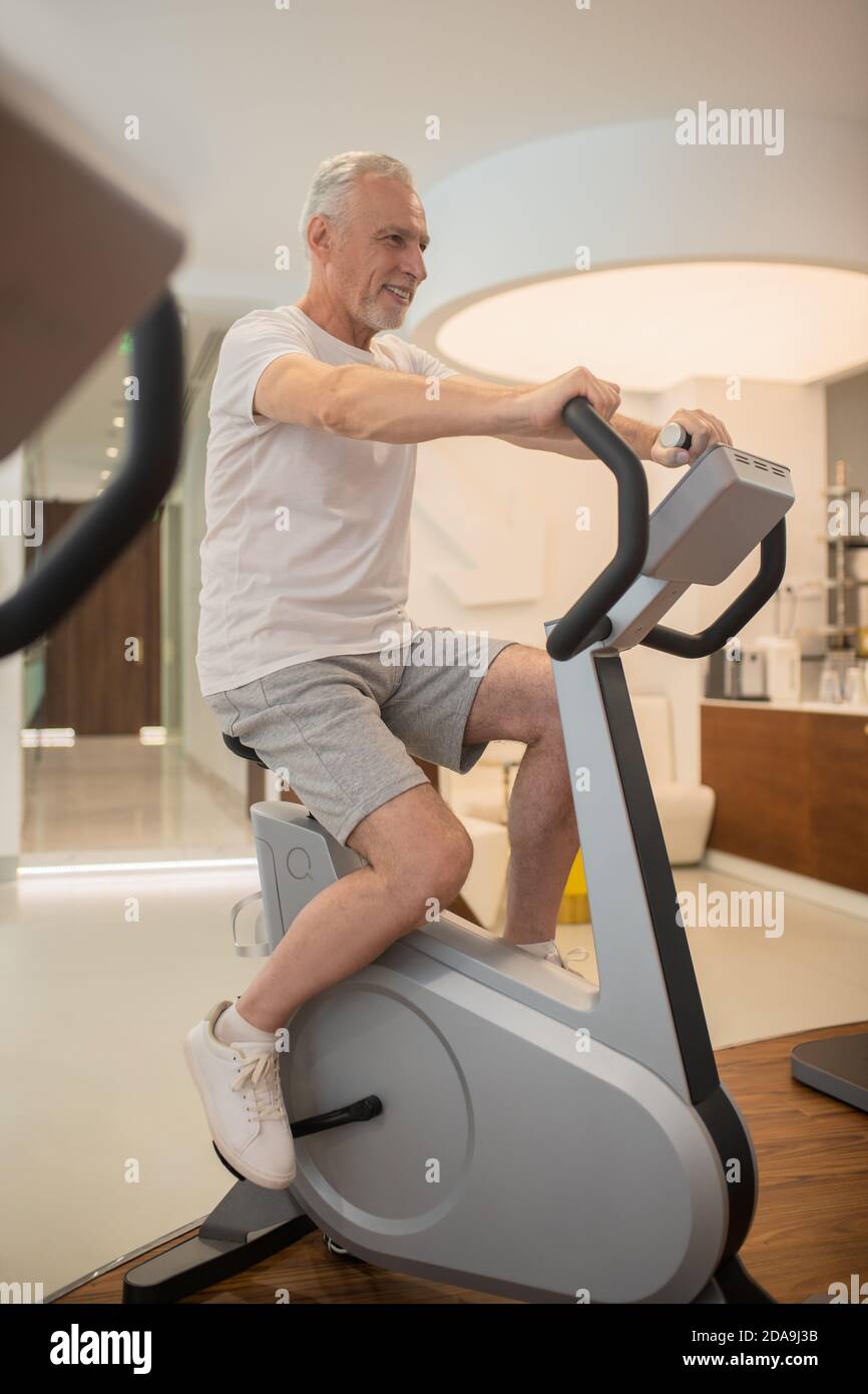 Grey-haired man sitting on a treadmill looking concentrated Stock Photo ...