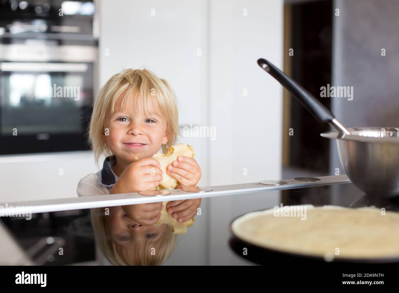 Cute toddler child, blond boy, making pancake in kitchen, eating them ...