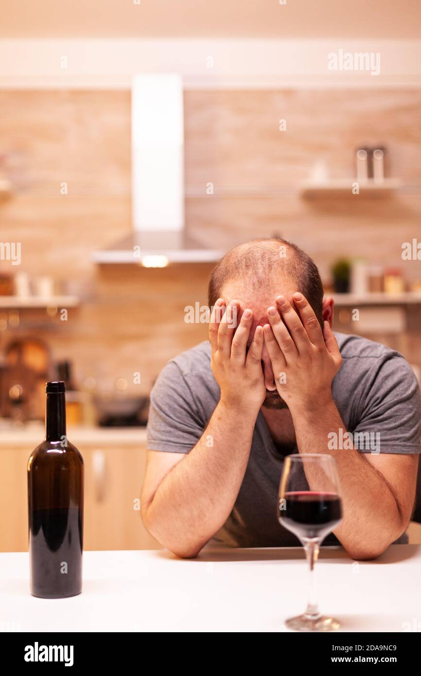 Frustrated drunk young man at home during life crisis with a bottle of ...