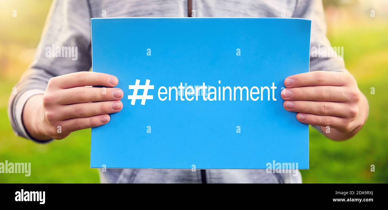 Male teenager holds a banner with the word entertainment against nature ...