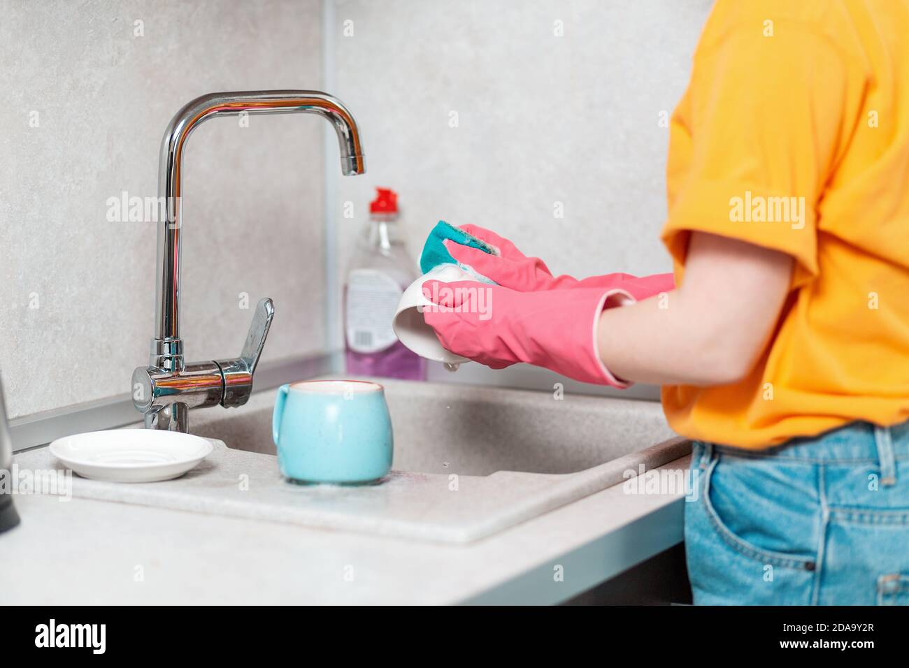 A housewife in casual clothes and pink rubber gloves is washing a cup ...