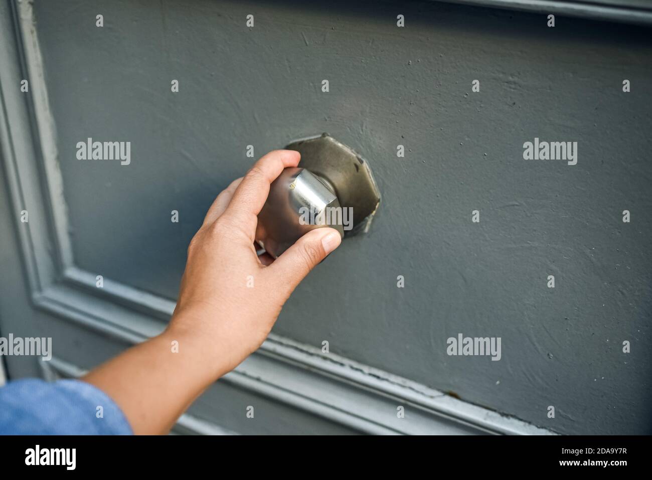 female hand holding the door handle . gray street door entrance to the ...