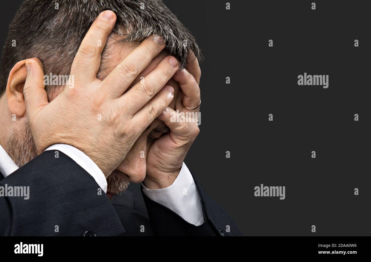 Headache. Portrait of an elderly man with face closed by hands on dark ...