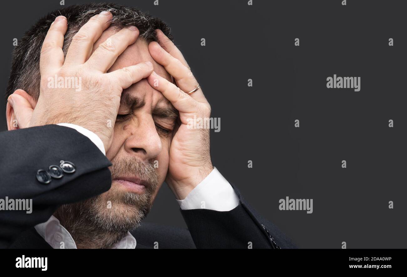 Headache. Portrait of an elderly man with face closed by hands on dark ...
