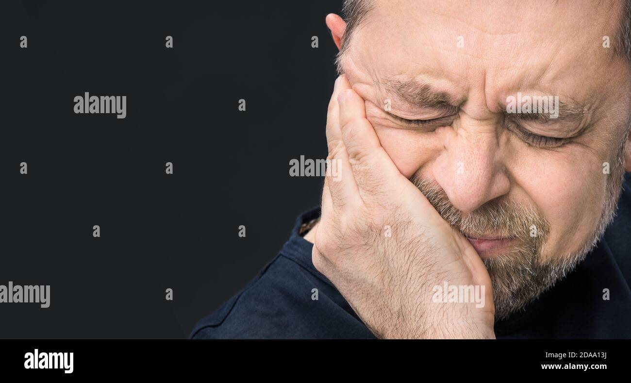 Headache. Portrait of an elderly man with face closed by hand on dark ...