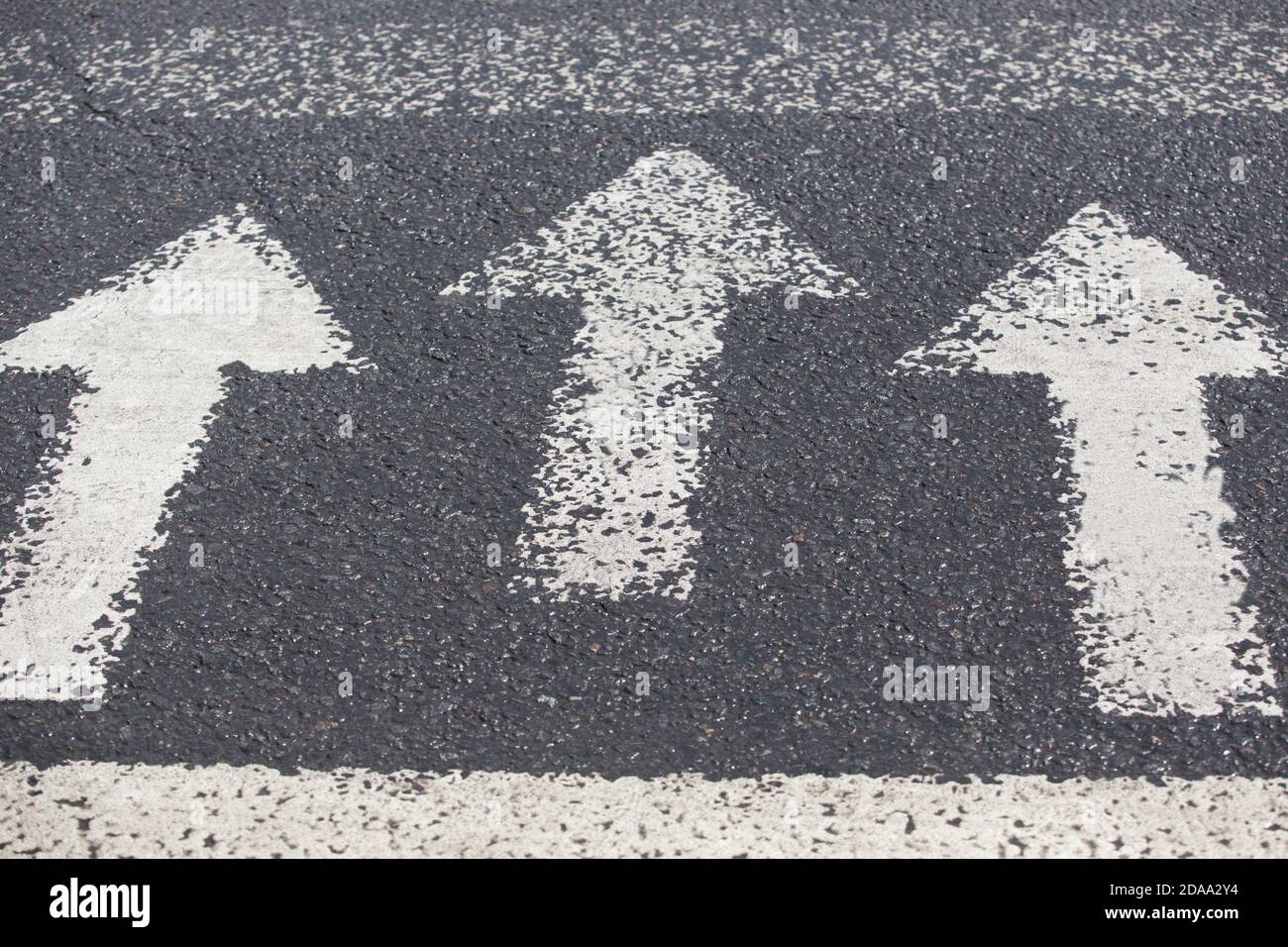 Three white arrows pointing in one direction on gray asphalt floor ...
