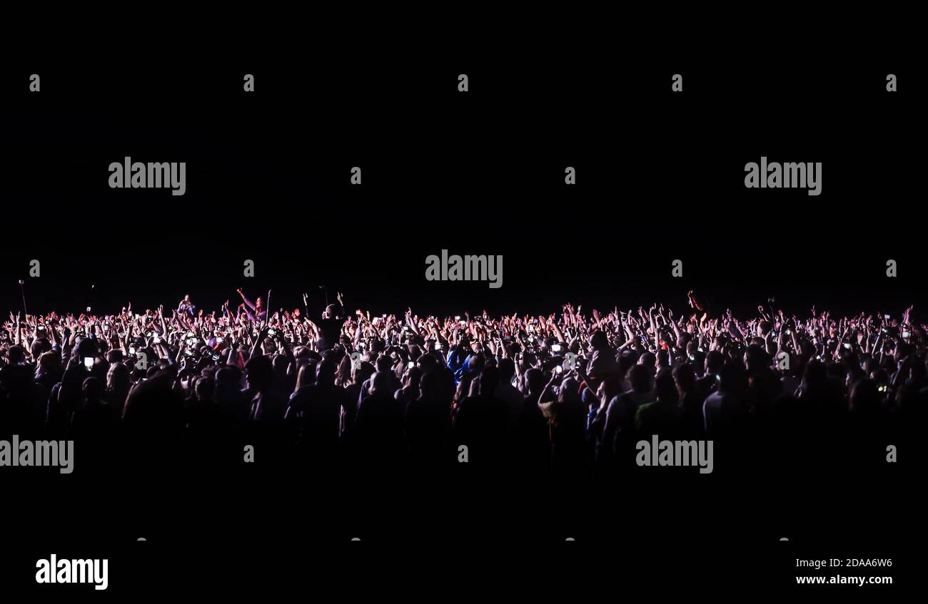 Crowd of spectators at a concert at night lit by a spotlight from the ...