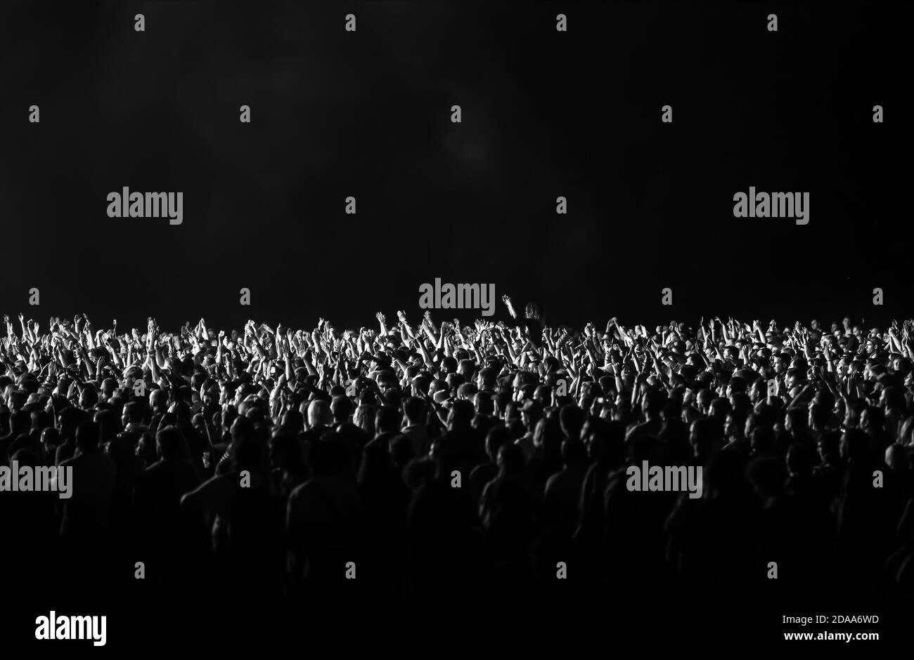 Crowd of spectators at a concert at night lit by a spotlight from the ...