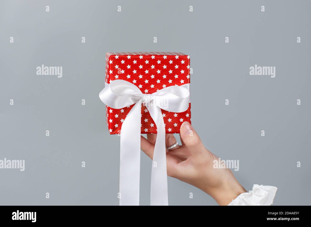 Hand holding wrapped gift box over grey background Stock Photo - Alamy