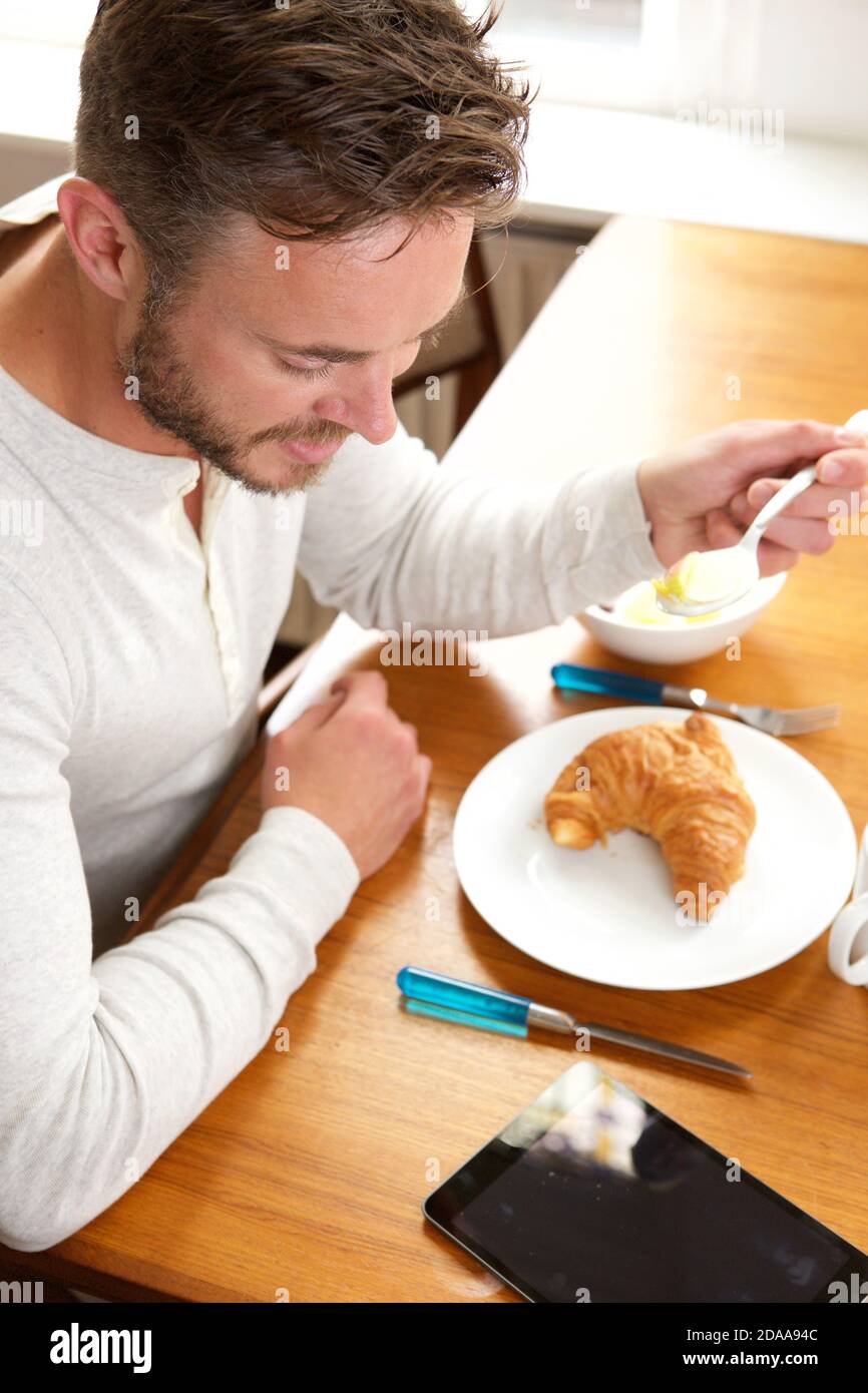 Portrait of handsome man eating breakfast and looking at tablet Stock ...