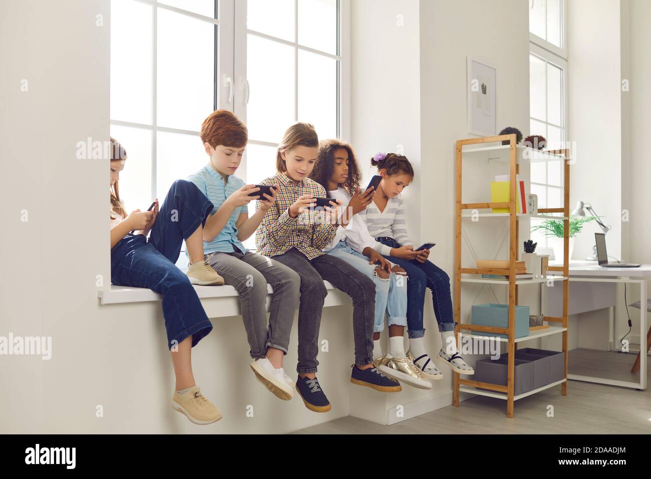 Kids sitting on windowsill, playing games on mobile phones and ignoring ...