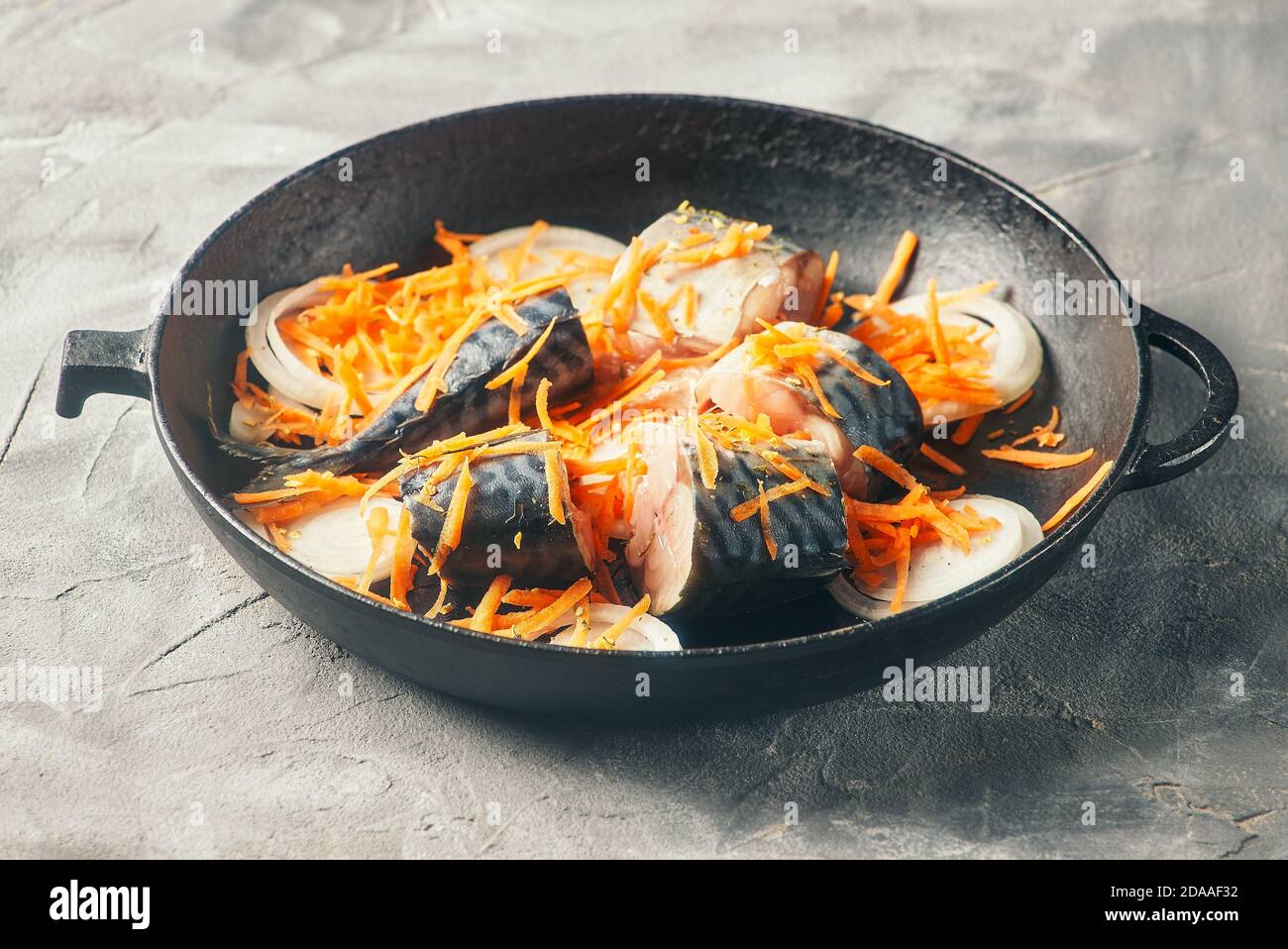 grated carrots and sliced fresh mackerel fish lie in a frying pan for ...